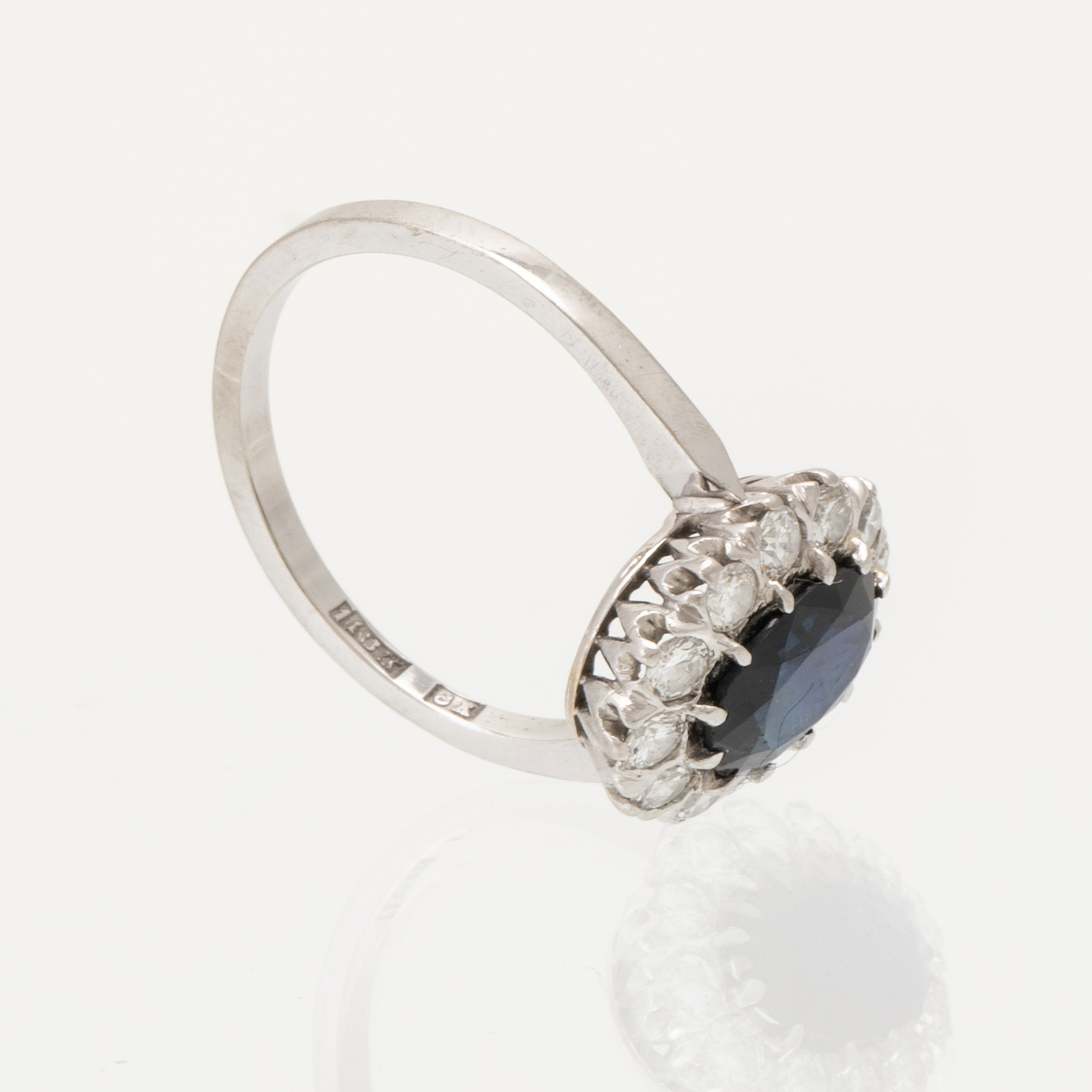 An 18K white gold ring set with an oval faceted sapphire and round ...